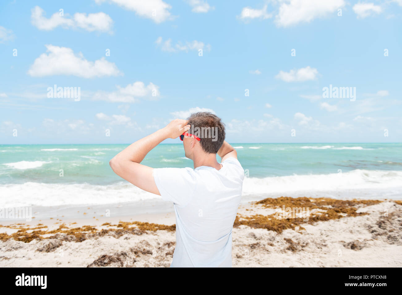 Back of young man in sunglasses standing on sand, sandy beach in Miami ...