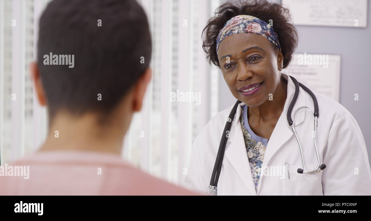 Positive female African doctor talking to male patient inside medical ...