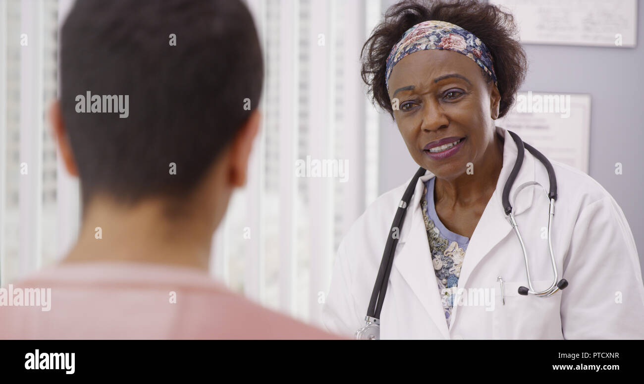 Positive female African doctor talking to male patient inside medical ...