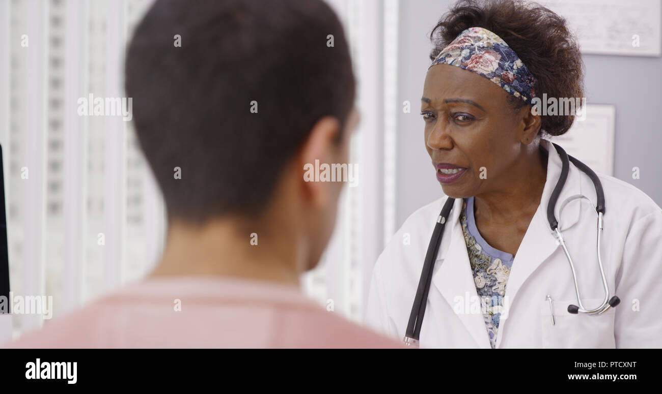 Positive female African doctor talking to male patient inside medical ...