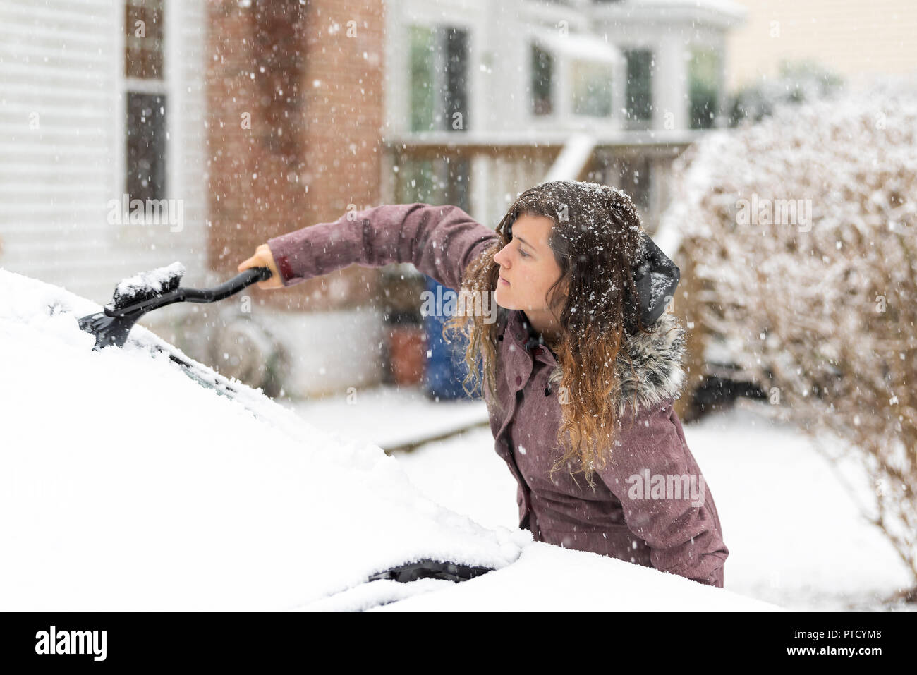 One young woman cleaning car windshield from snow, ice with brush and ...