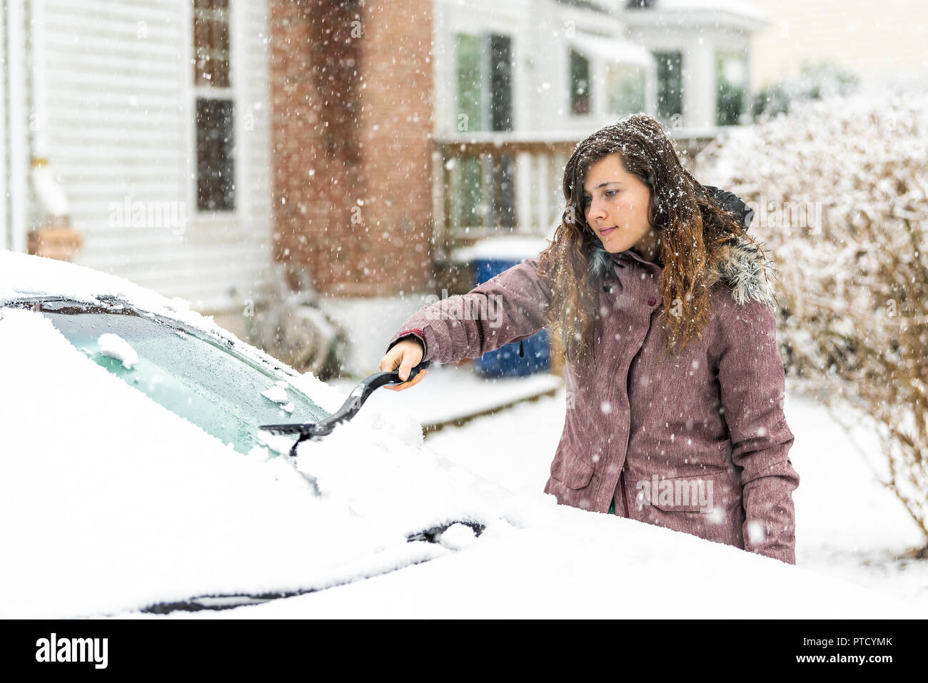 One young woman cleaning car windshield window from snow, ice with ...