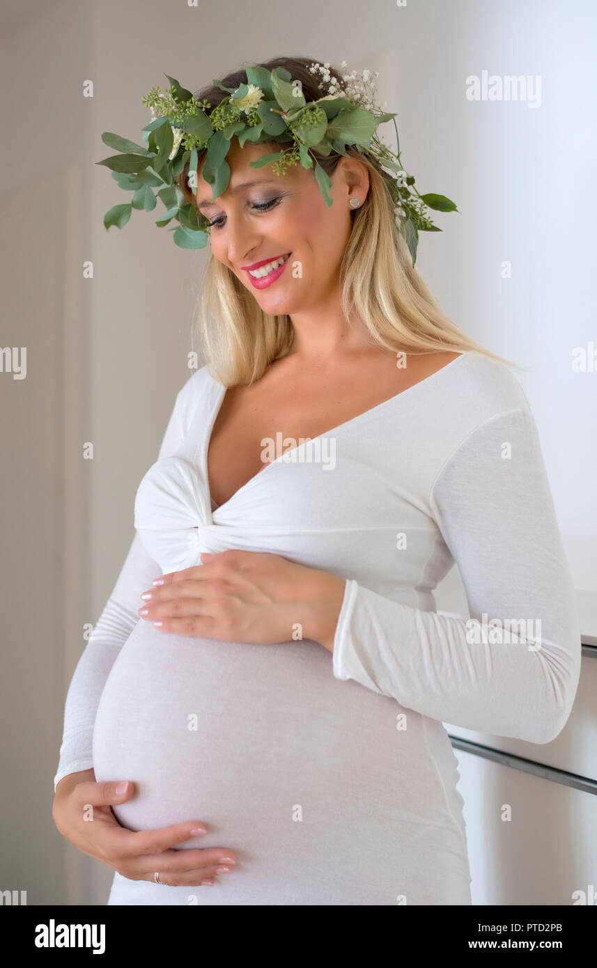Woman, bride, with wreath of flowers, nine months pregnant, holding ...