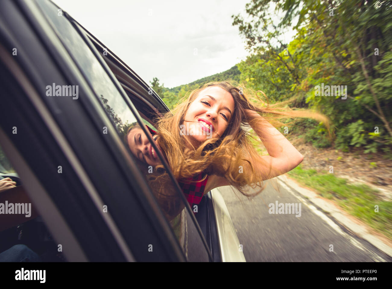 A girl is with her head out of a car window while is driving in nature ...