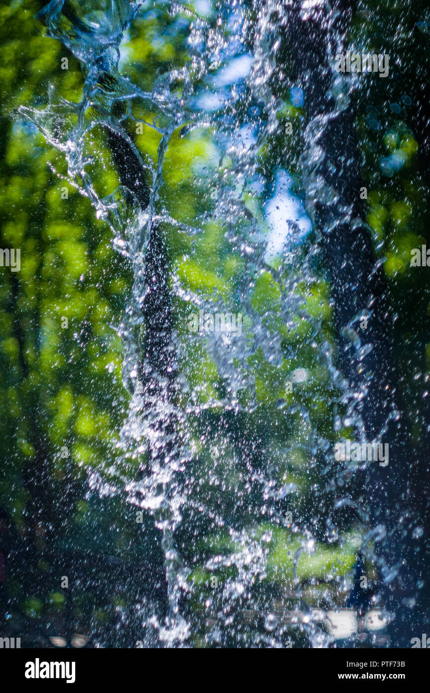transparent falling water vertical flows against a blue sky and green ...
