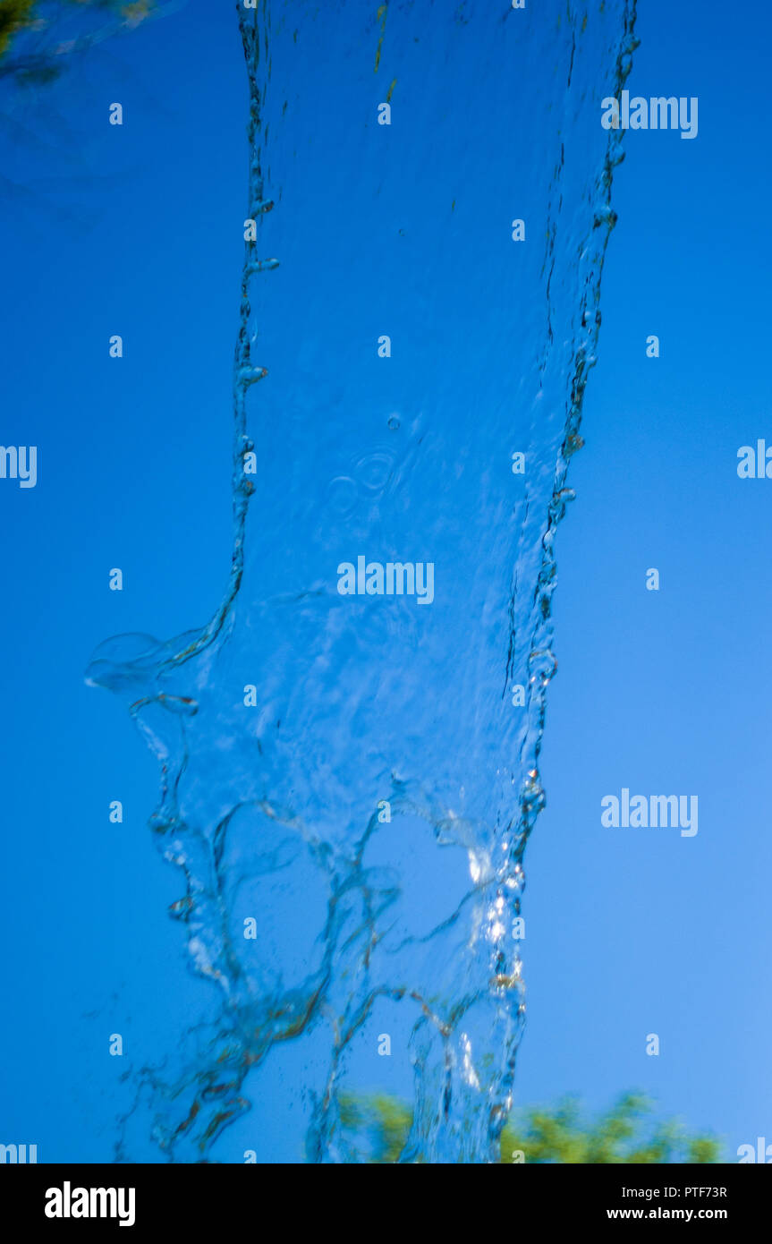 transparent falling water vertical flows against a blue sky and green ...