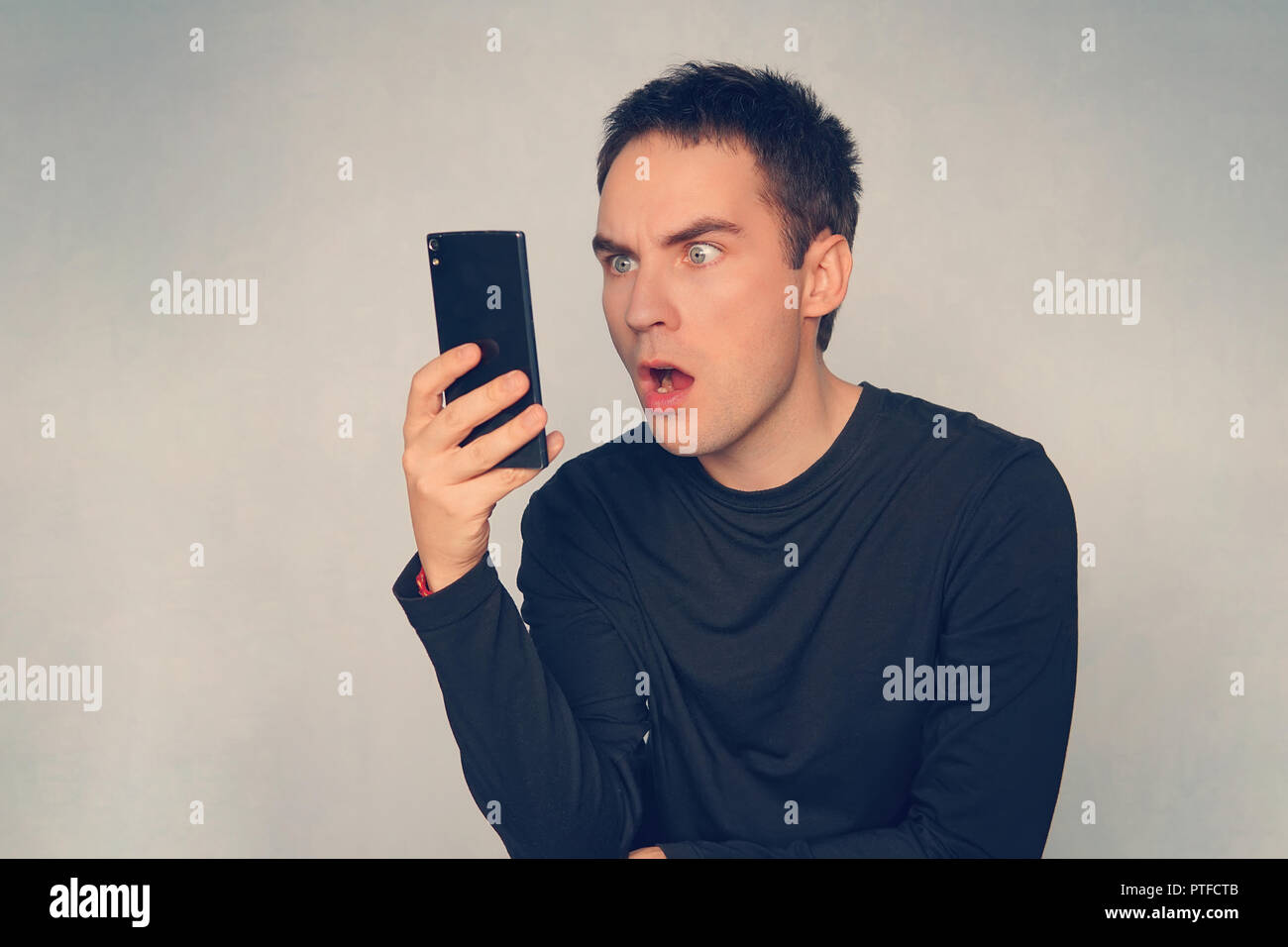 Studio shot of young man using mobile phone looking shocked while ...