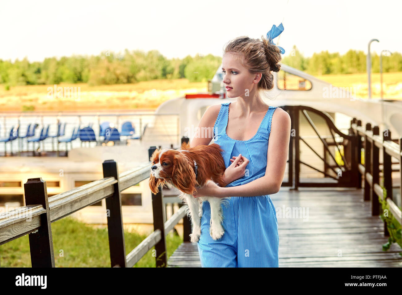 Young girl in stylish clothes walking along pier,holding cute cocker ...