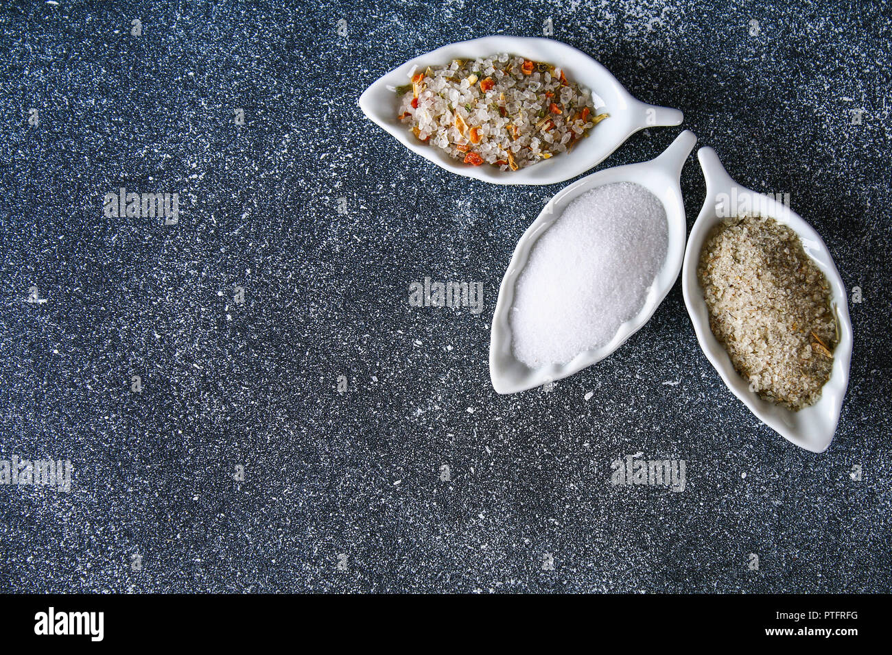 Different types of salt in glass bowls on a dark gray table. Background ...