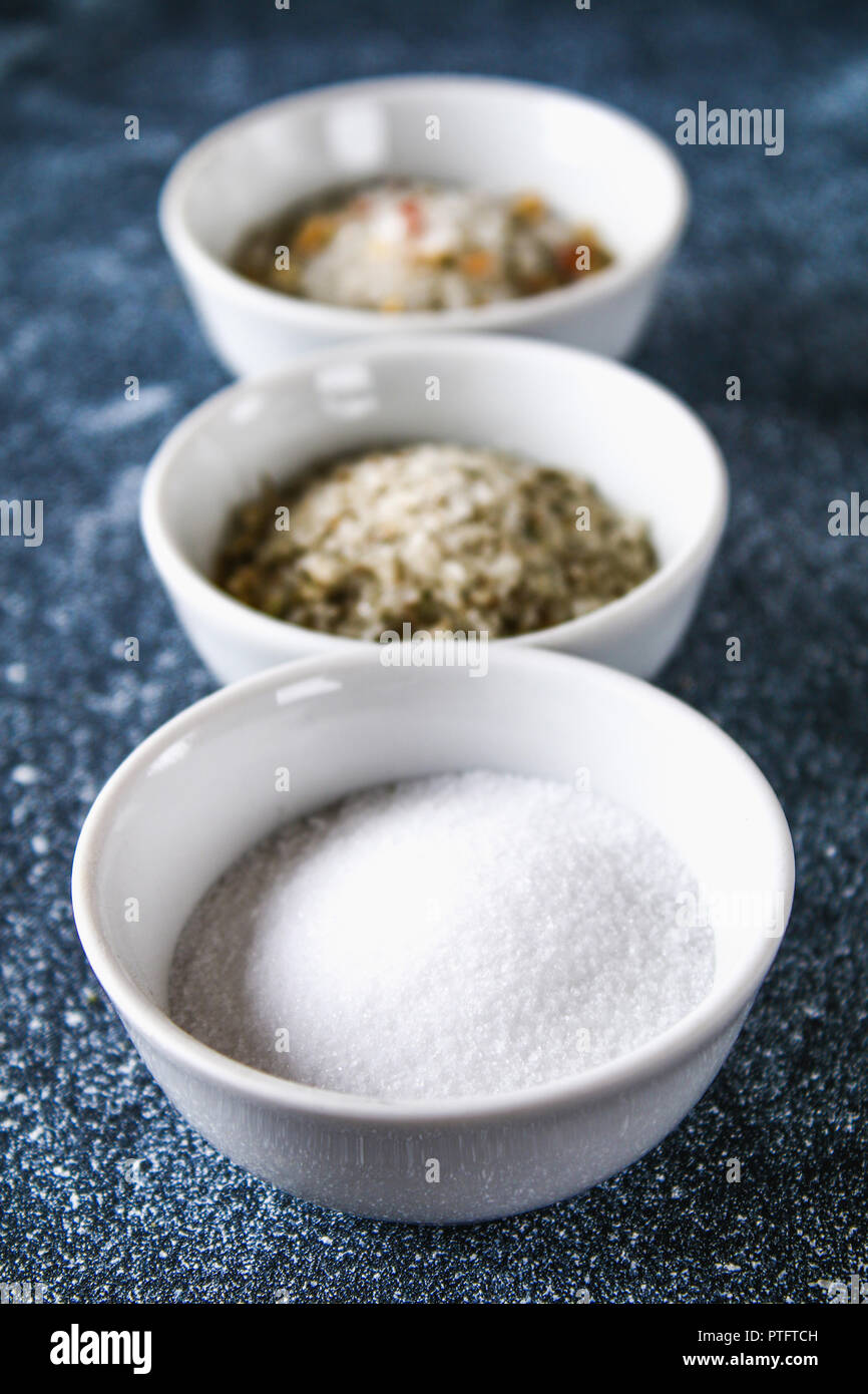 Different types of salt in glass bowls on a dark gray table. Background ...