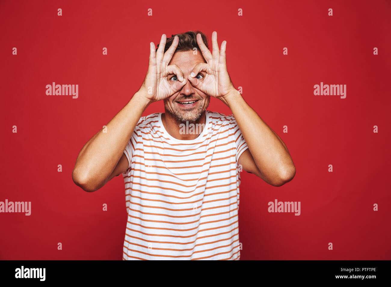 European man in striped t-shirt smiling and looking through holes made ...