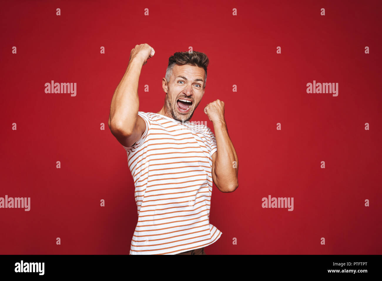 Cheerful man 30s in striped t-shirt screaming and clenching fists ...