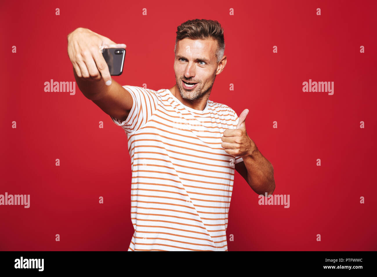 Portrait of a cheerful man standing over red background, taking a ...