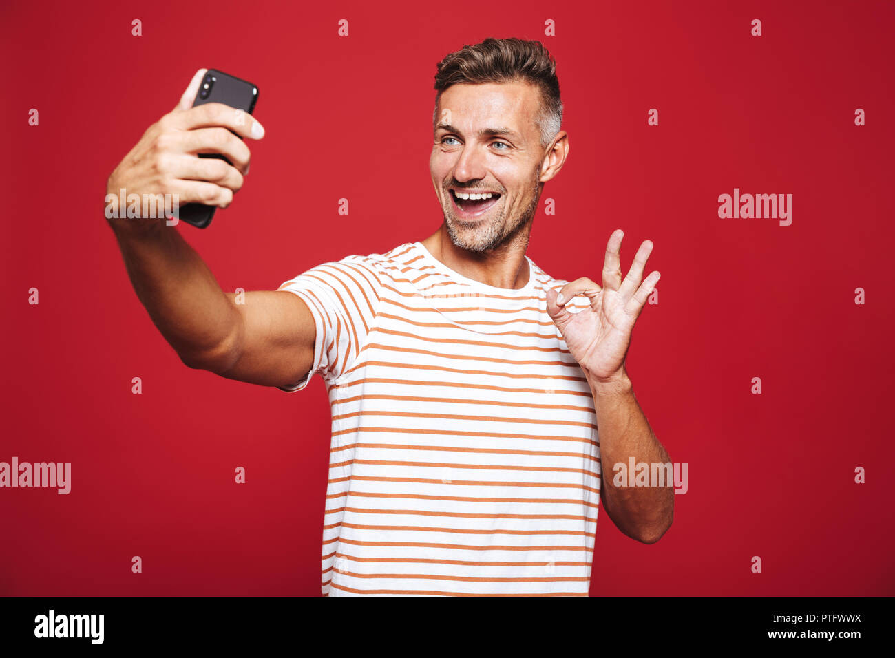 Portrait of a cheerful man standing over red background, taking a ...