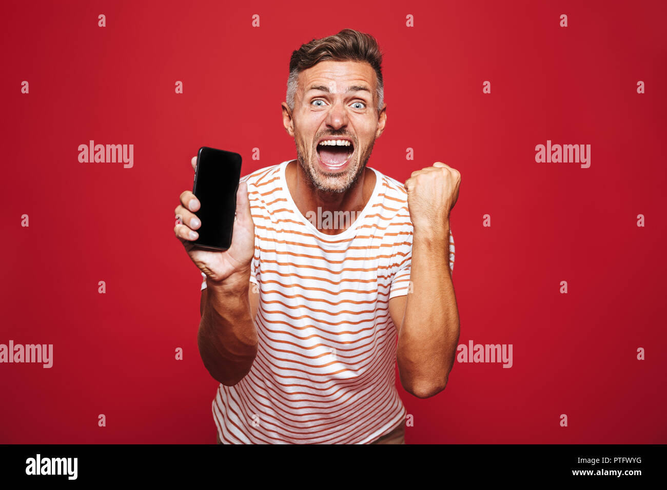 Portrait of an excited man standing over red background, showing mobile ...
