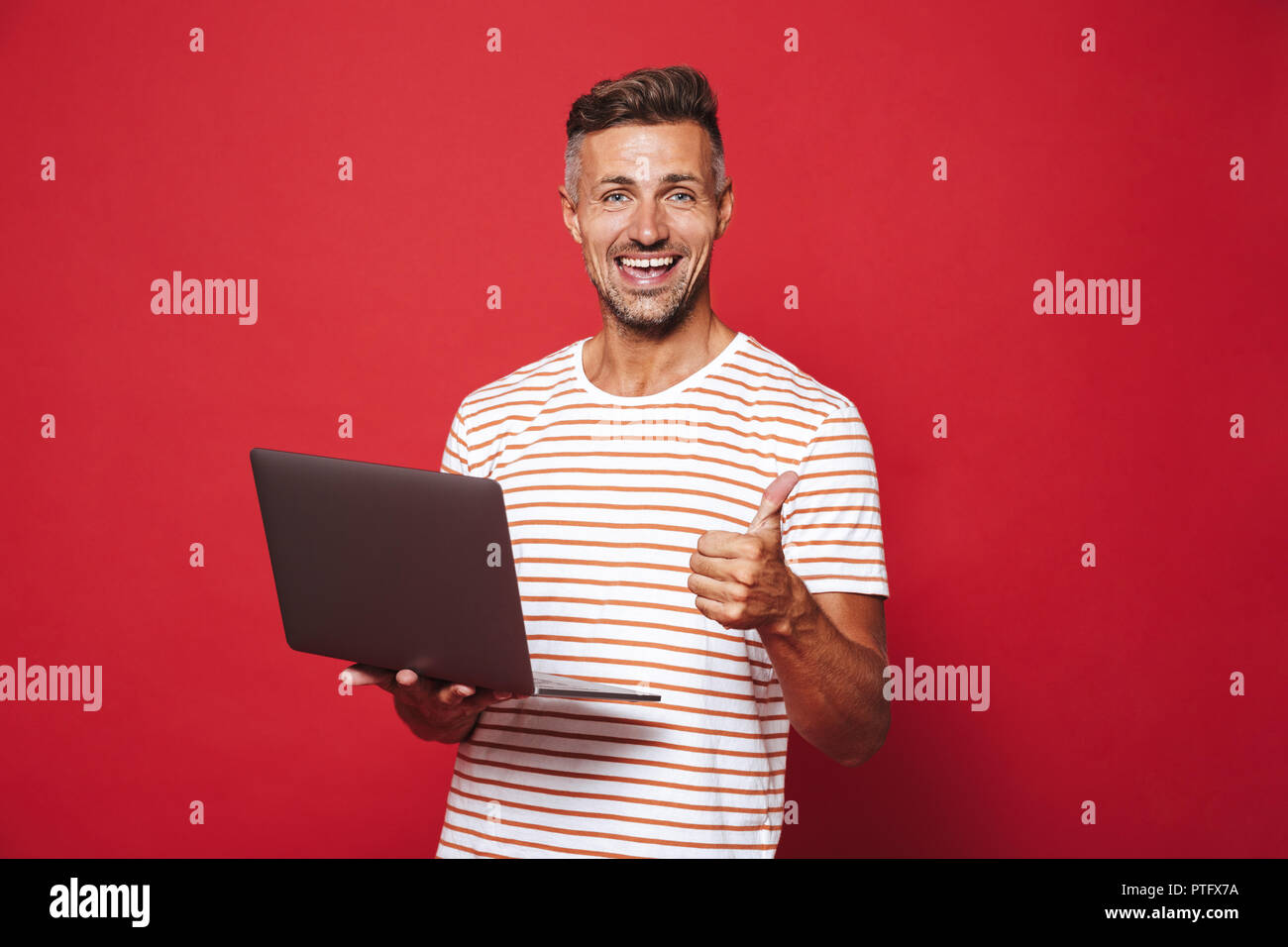 Optimistic unshaved man in striped t-shirt smiling and holding gray ...