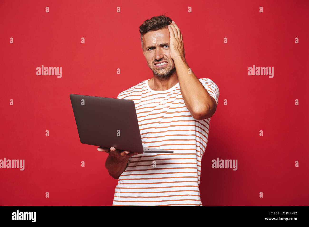 Image of confused young man in striped t-shirt smiling and holding gray ...