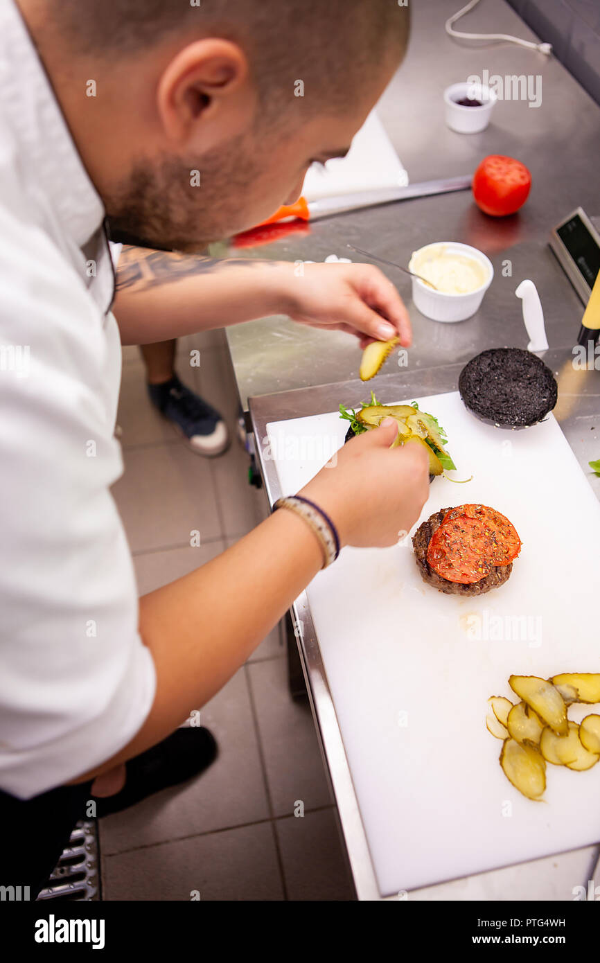 Chef puts pickles on delicious burger meat. In restaurant kitchen Stock ...