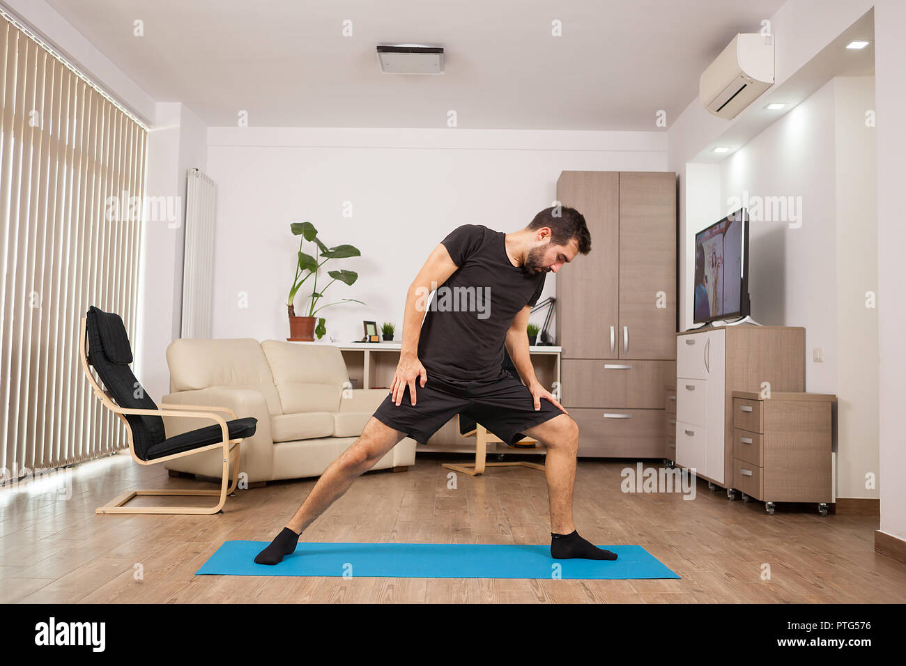 Bearded man doing Warrior II yoga posing and stretching his muscles ...