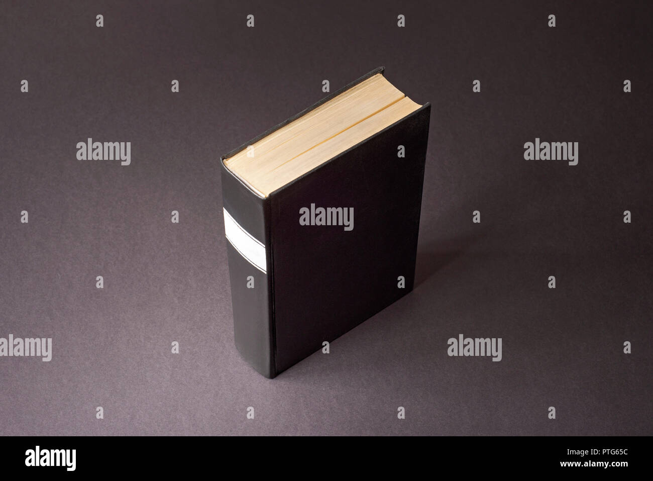 Black book with white frame on spine standing a dark paper surface ...