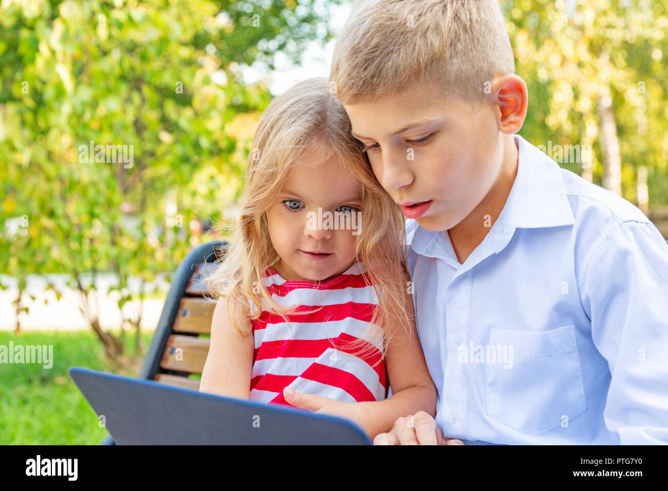 Smiling brother and sister sitting on bench in park and playing on ...