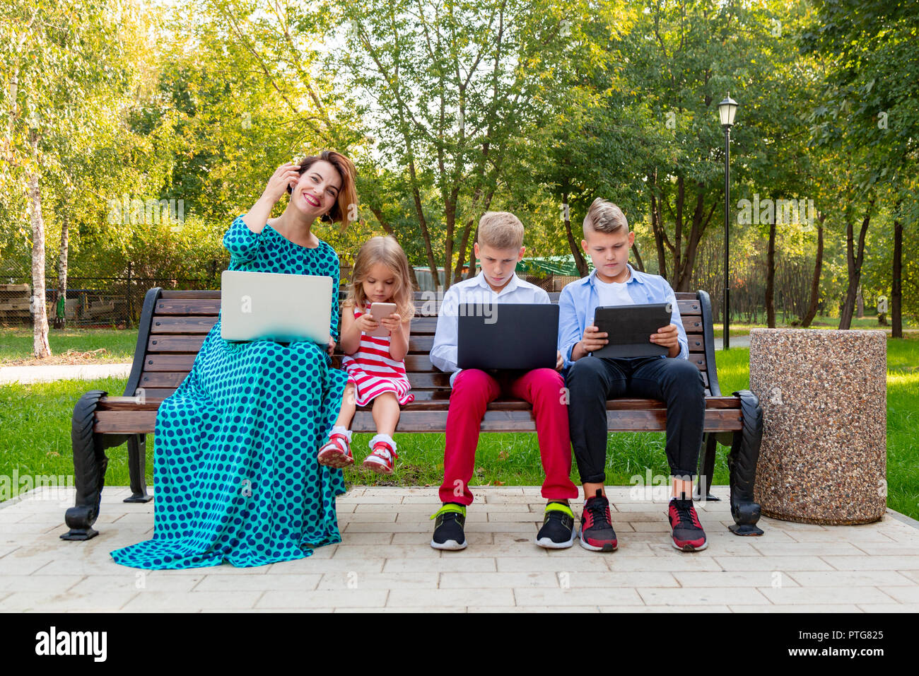 Young family with gadgets sitting on the bench Stock Photo - Alamy