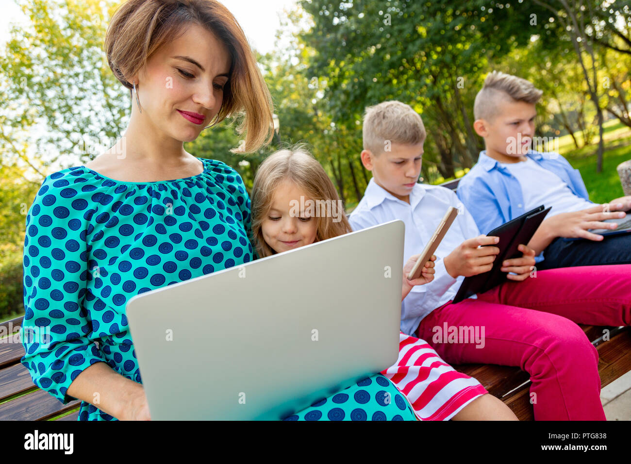 Young family with gadgets sitting on the bench Stock Photo - Alamy