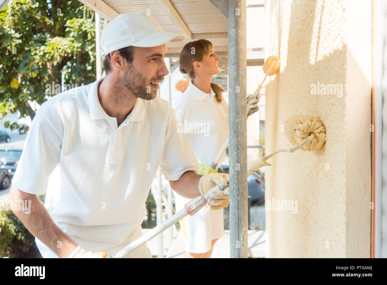 Painter and colleague painting wall with roller, side view Stock Photo ...