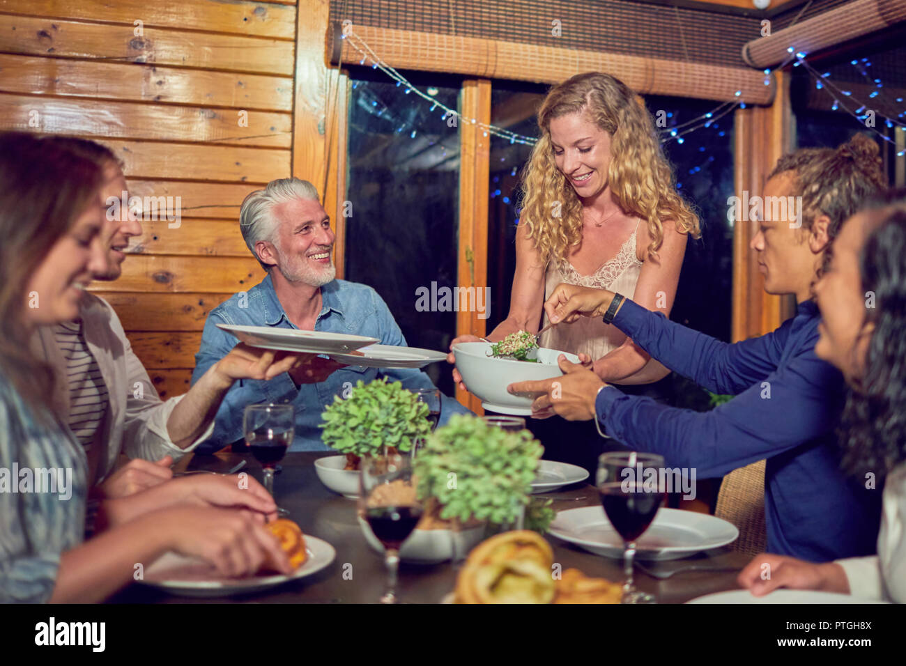 Woman serving dinner to friends at cabin dining table Stock Photo - Alamy