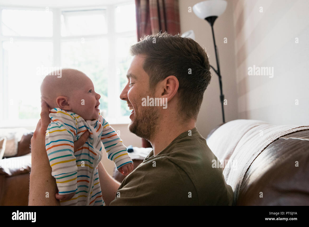 Father holding his new born baby boy up to his face to make him laugh ...