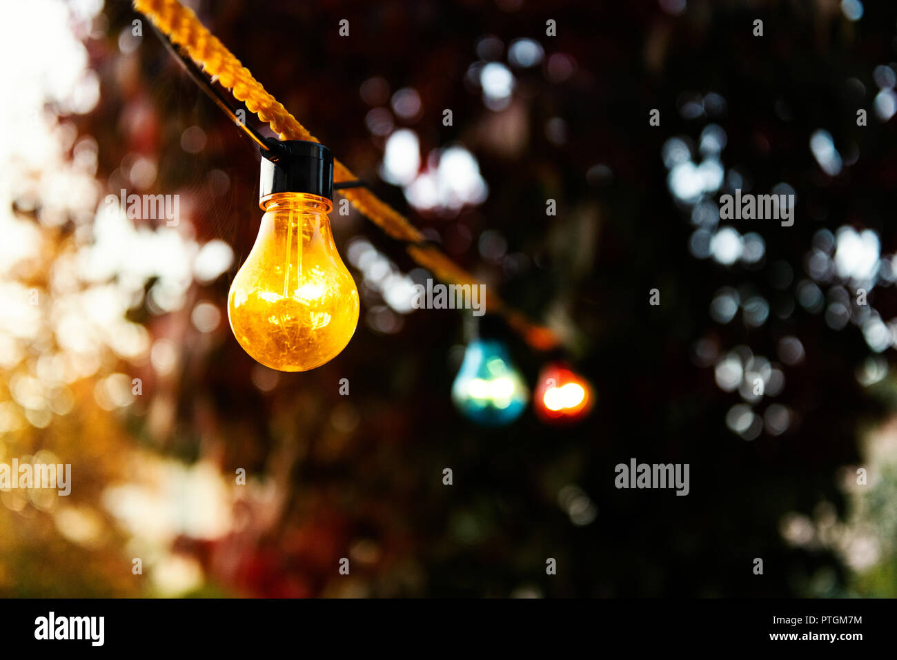 Yellow party light bulb shining on chain Stock Photo - Alamy