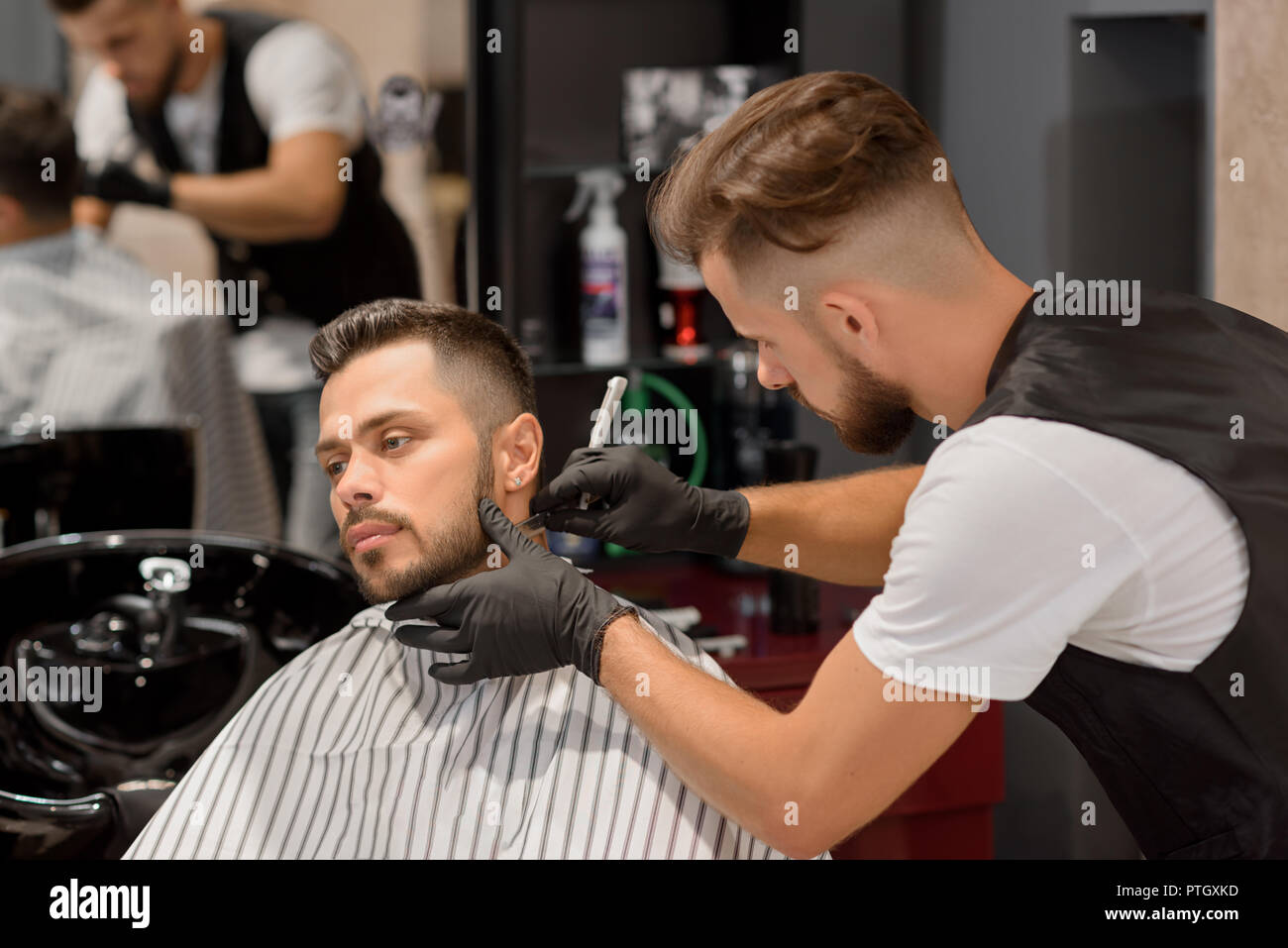 Barber concentrated on shaving man's beard using sharp razor. Client ...