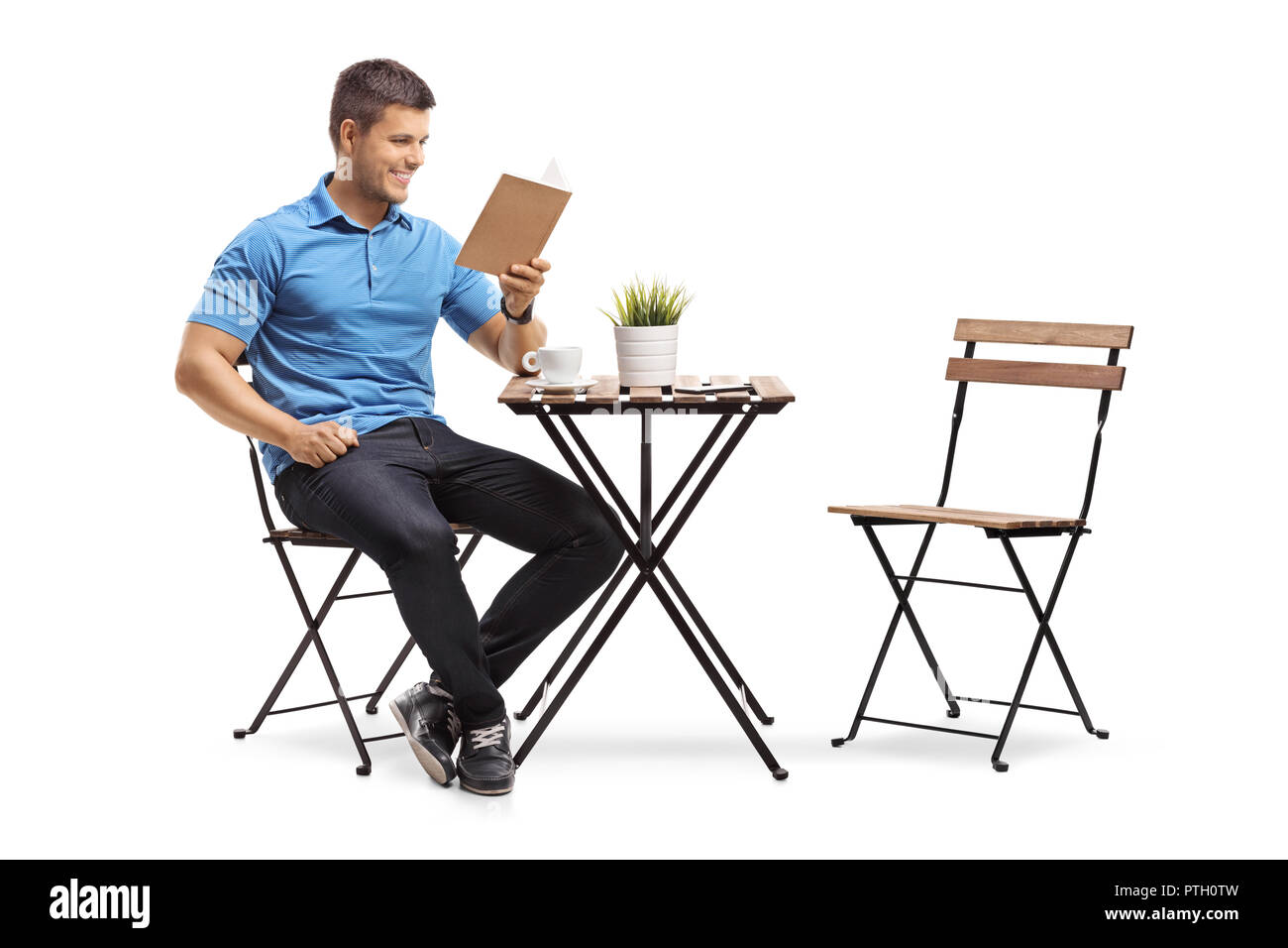 Young guy seated at a coffee table reading a book isolated on white ...