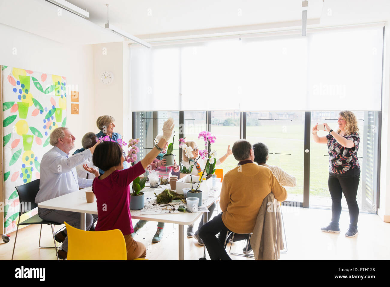 Instructor photographing active seniors enjoying flower arranging class ...