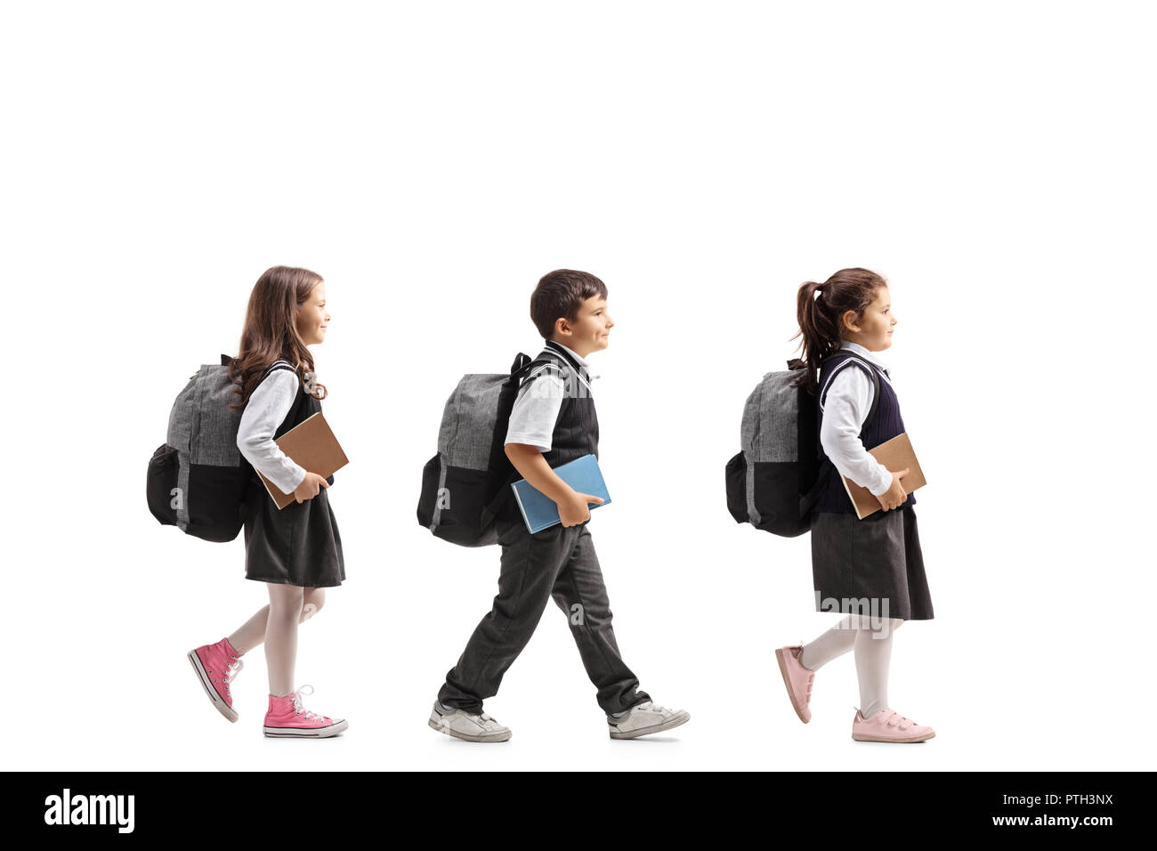 Full length profile shot of three schoolchildren with backpacks and ...