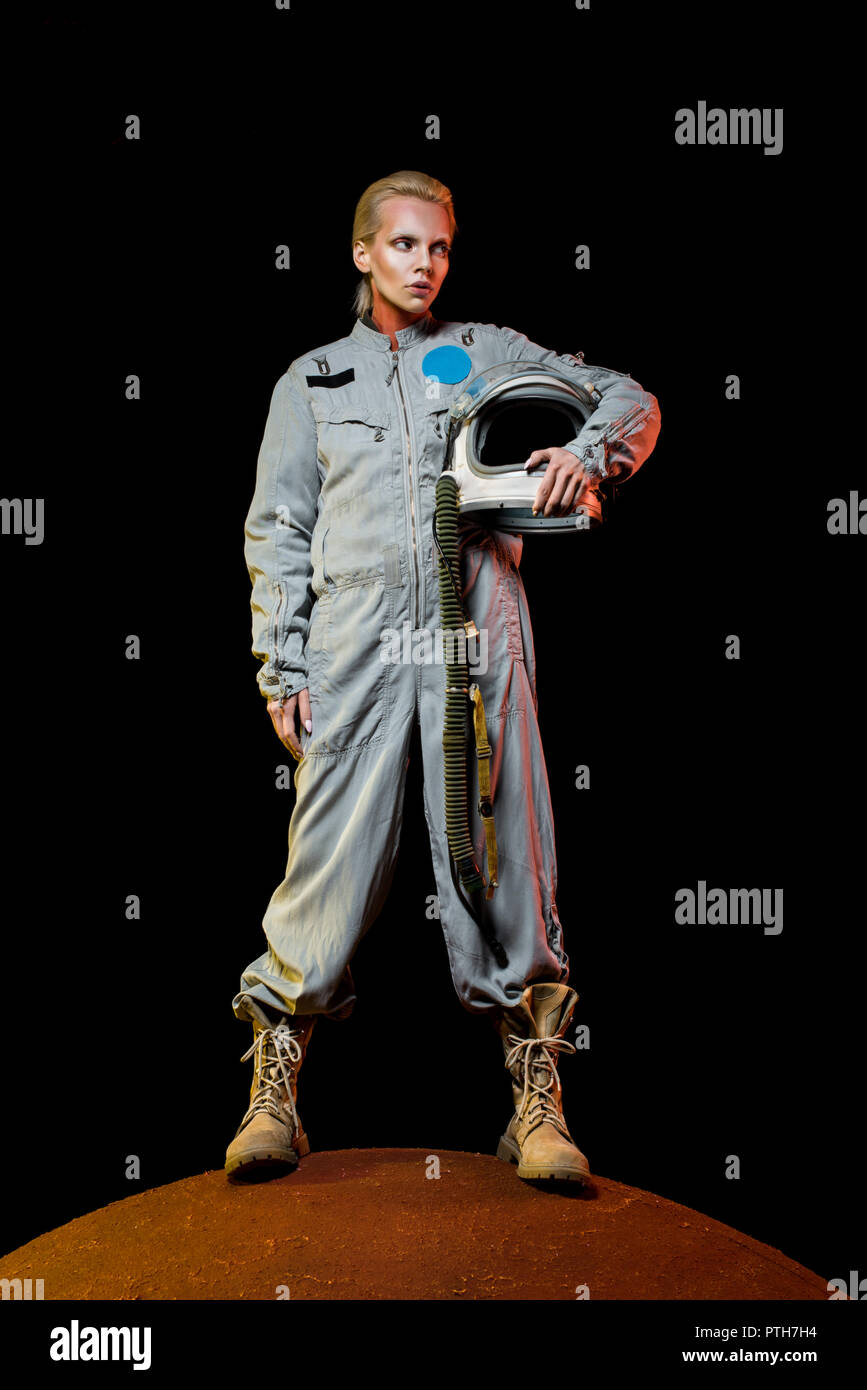 attractive female cosmonaut in spacesuit holding helmet and standing on ...