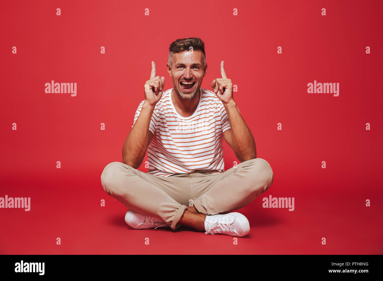Image of handsome man 30s in striped t-shirt pointing fingers upward ...