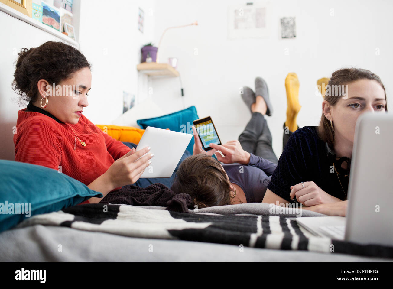 Young women friends hanging out, using smart phone, digital tablet and ...