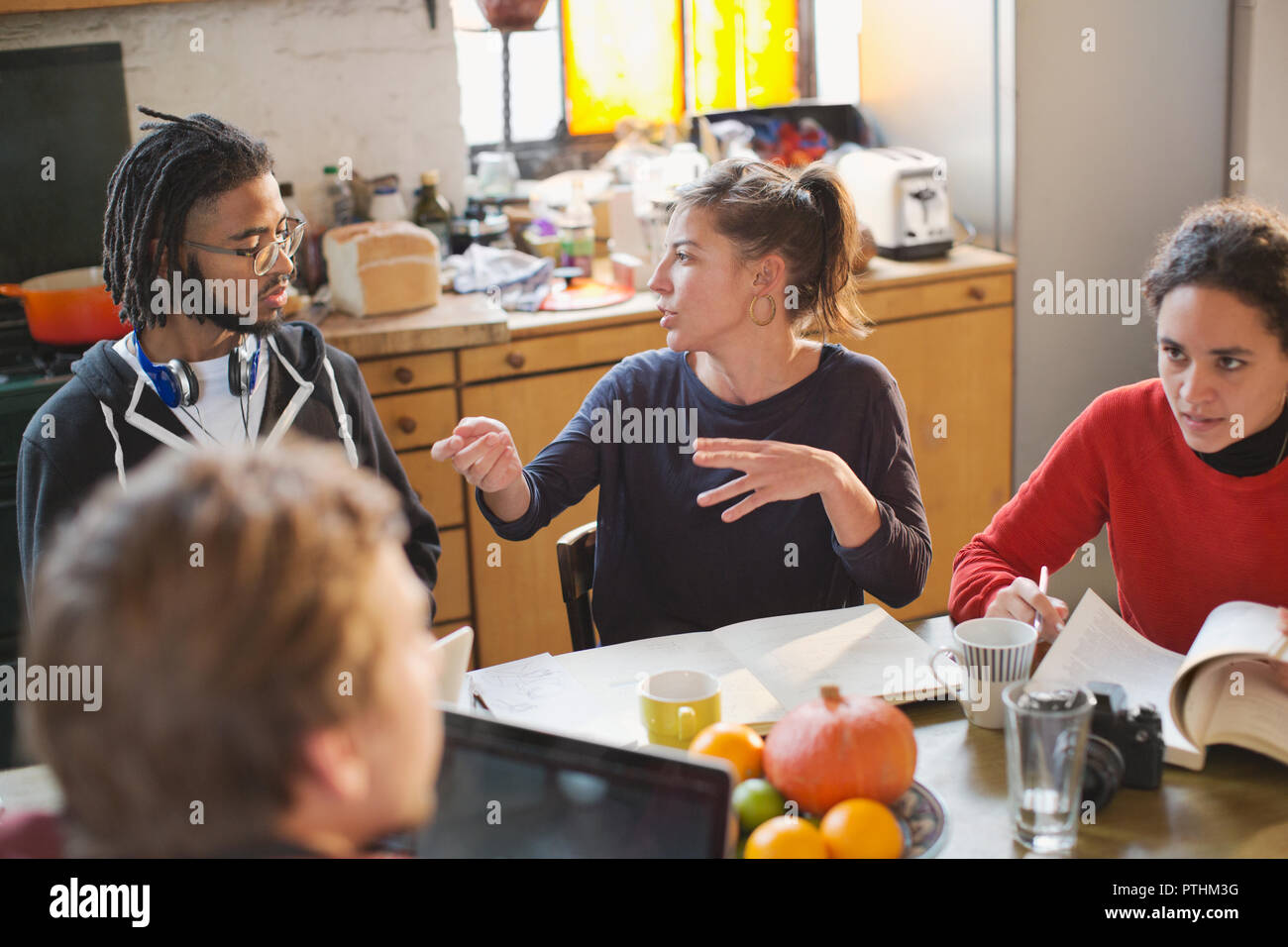 Young college student roommates studying, talking at kitchen table in ...