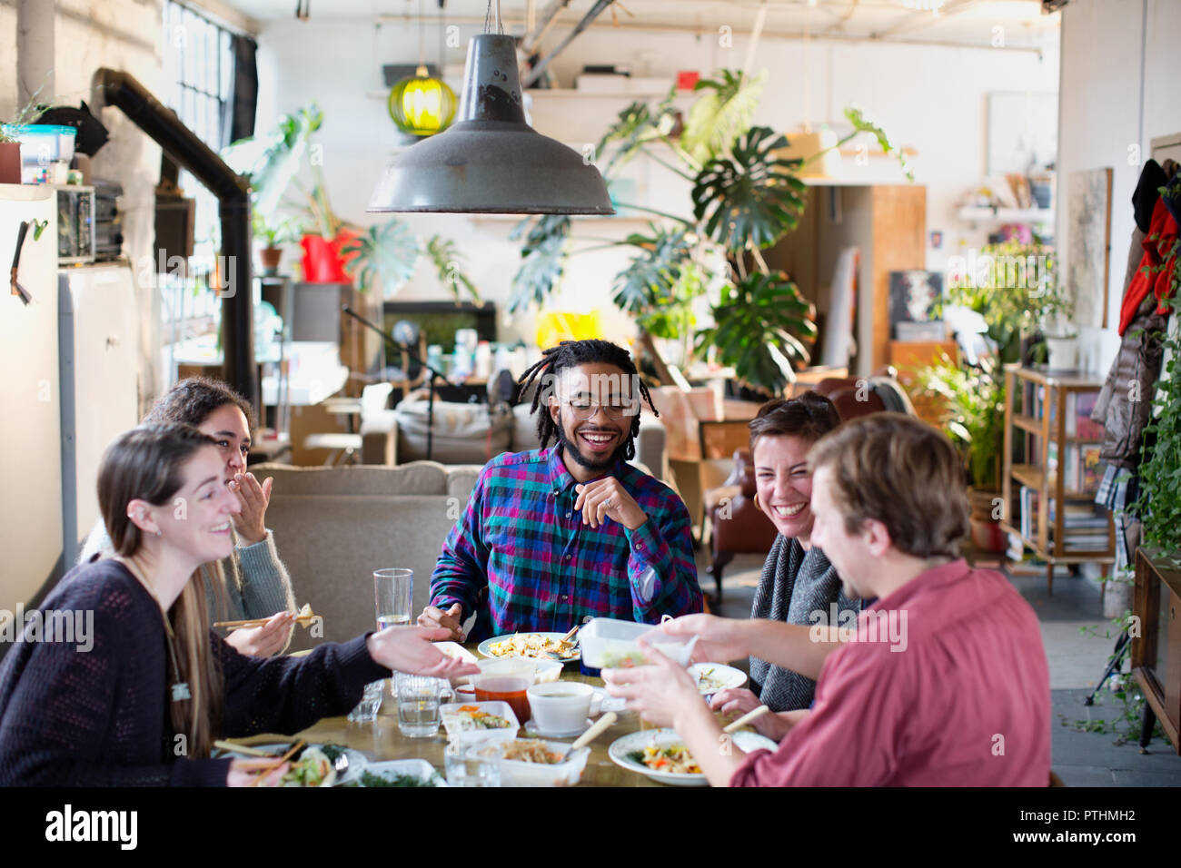 Young adult roommate friends enjoying takeout food at kitchen table in ...
