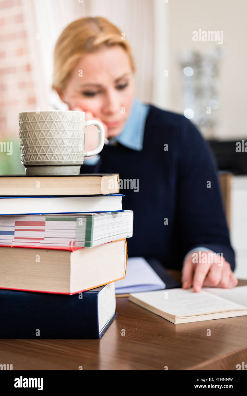 Stack of books with mug on top in front of woman reading book Stock ...