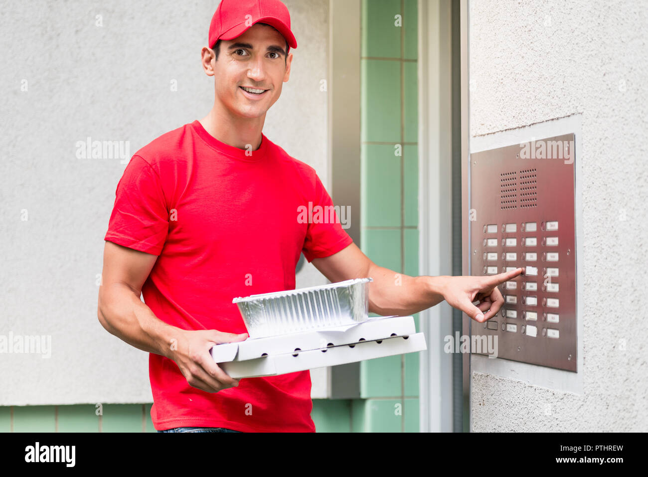 Pizza delivery man in red uniform carrying boxes using the intercom at ...