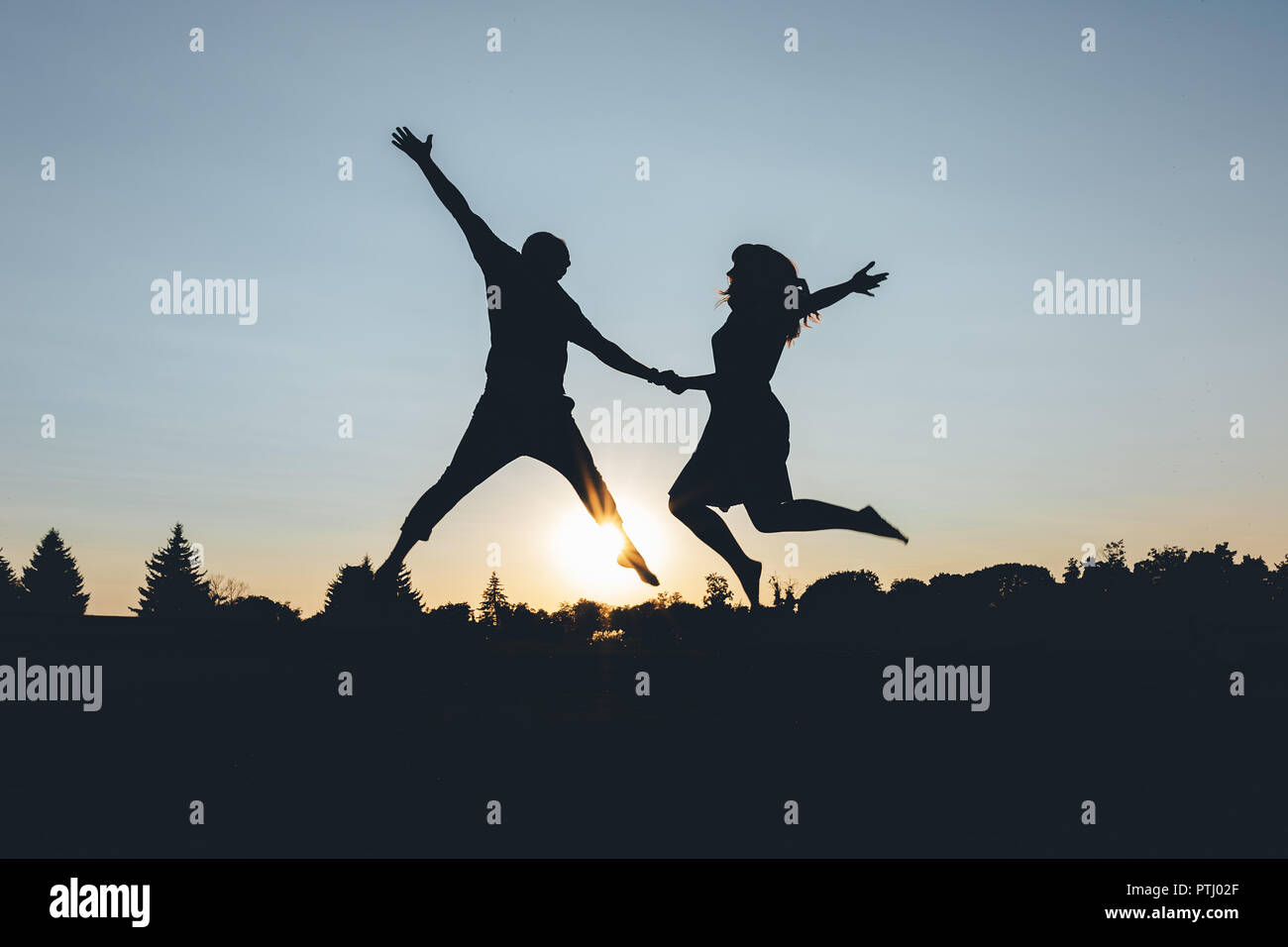 Jumping couple holding hands on sunset background Stock Photo - Alamy