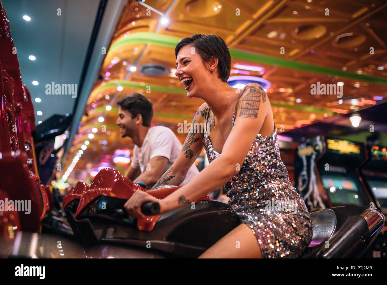 Excited woman playing a racing game sitting on an arcade racing bike ...