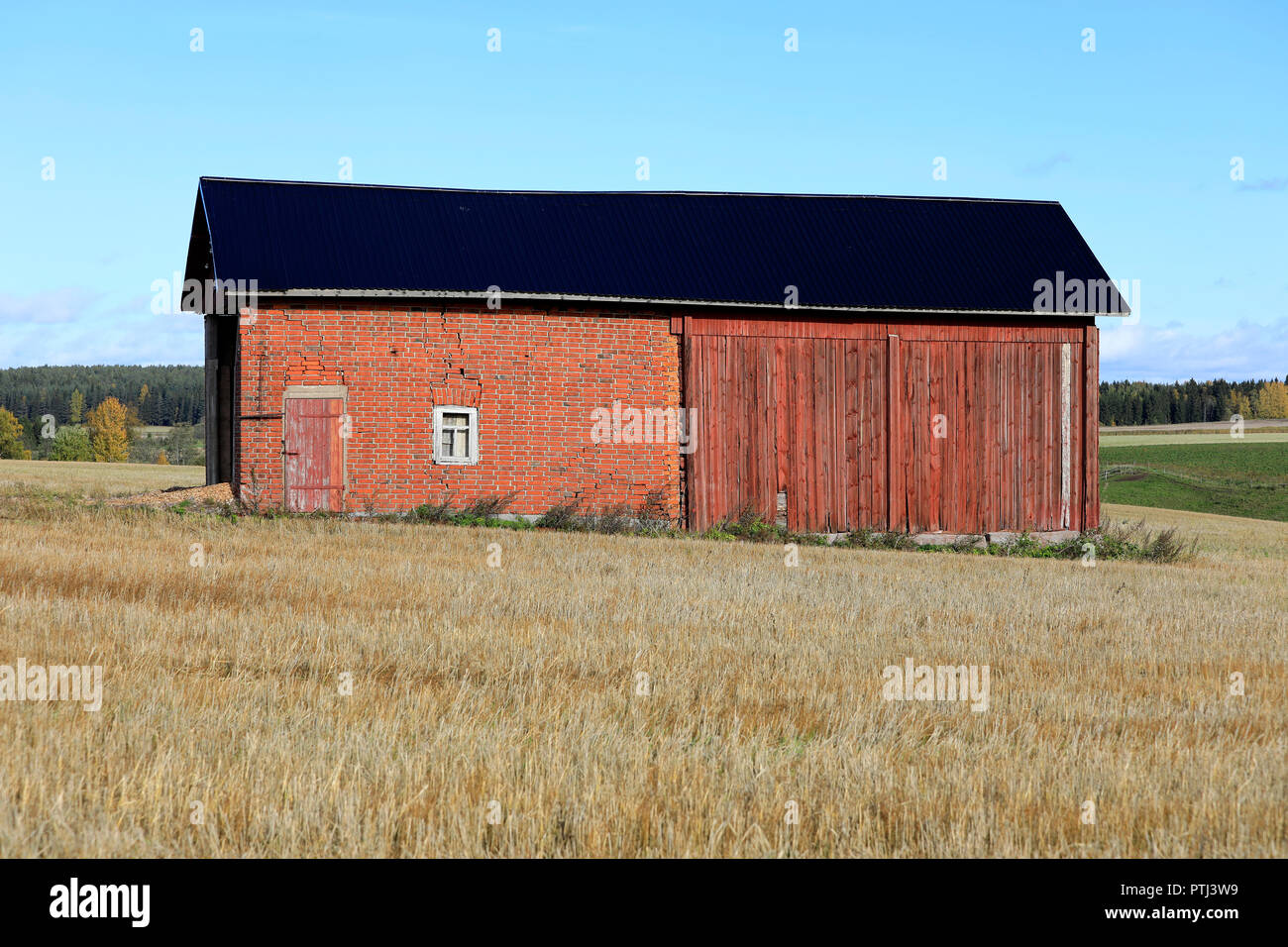 Old red farm building on stubble field with blue sky background on a ...