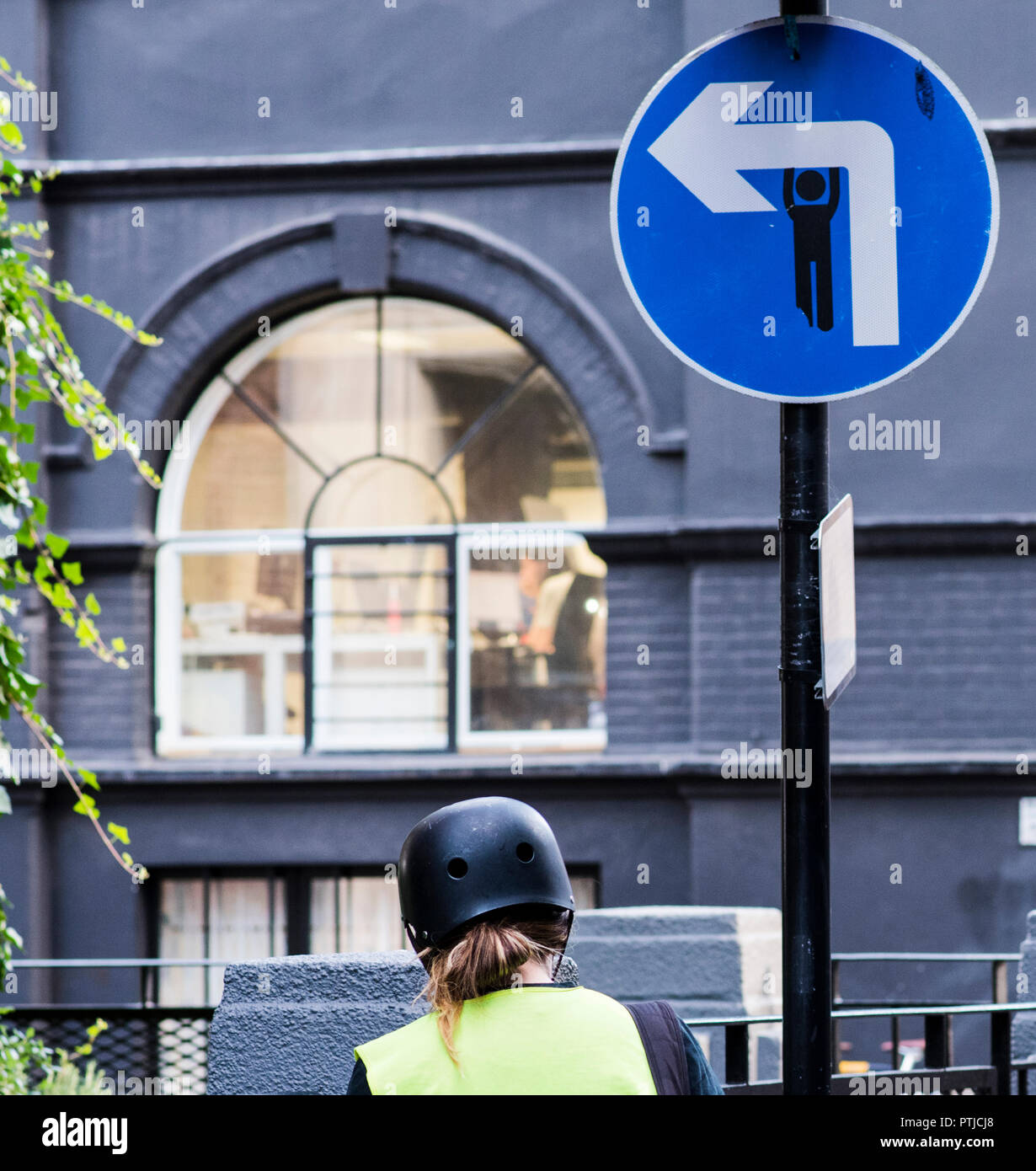 Woman cyclist wearing strange helmet stands underneath road sign with ...