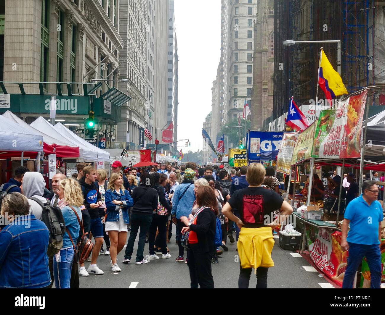 Crowd of people line the street in front of booths at a street fair on ...
