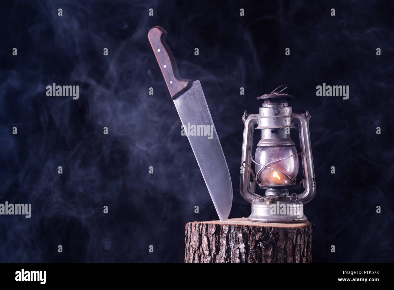 Big knife and burning old oil lamp on wood log in forest and black ...