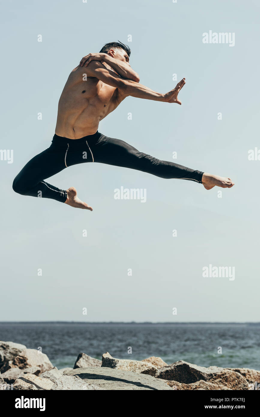 handsome shirtless dancer jumping over rocky seashore Stock Photo - Alamy
