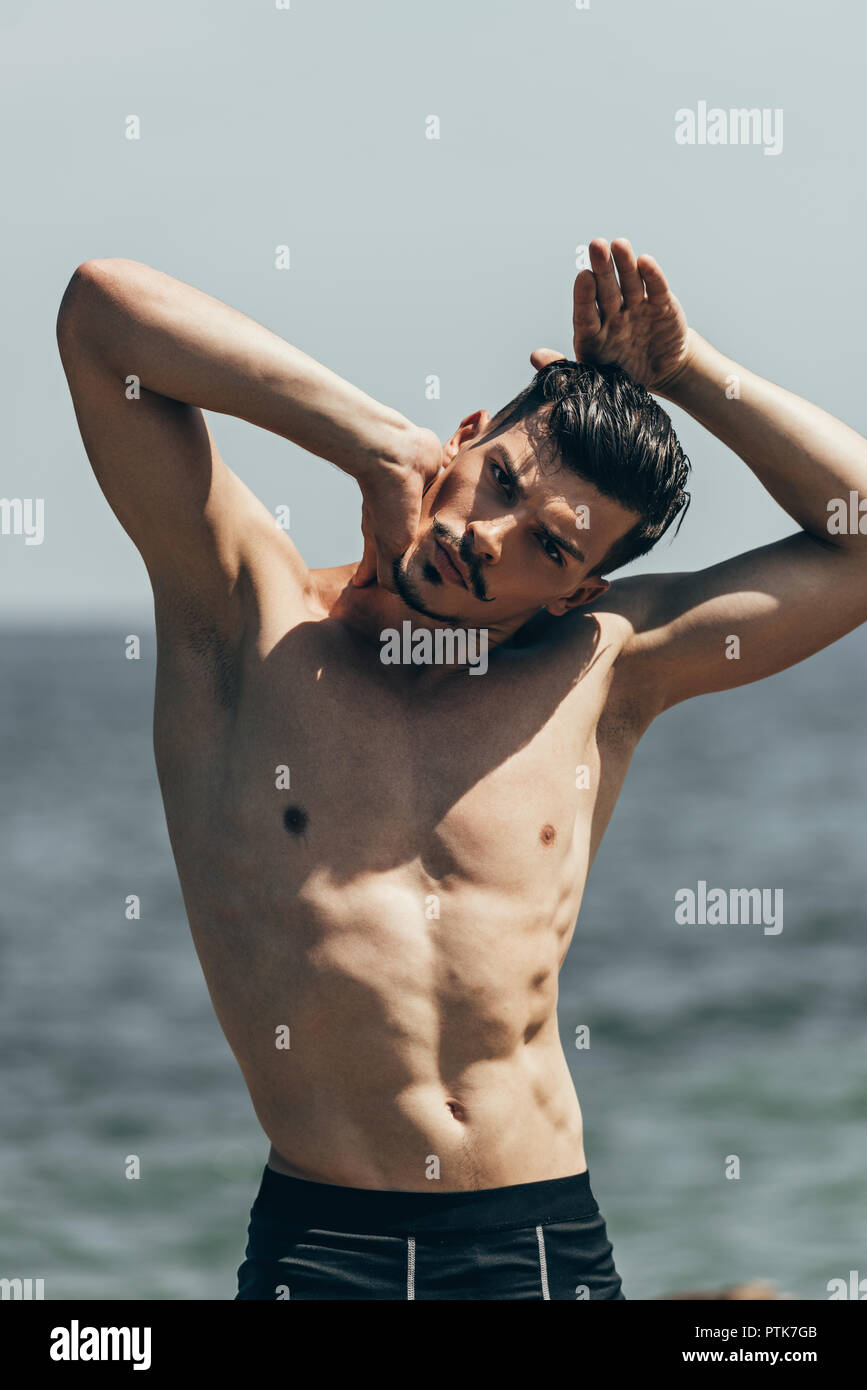 handsome shirtless man stretching neck before workout in front of sea ...